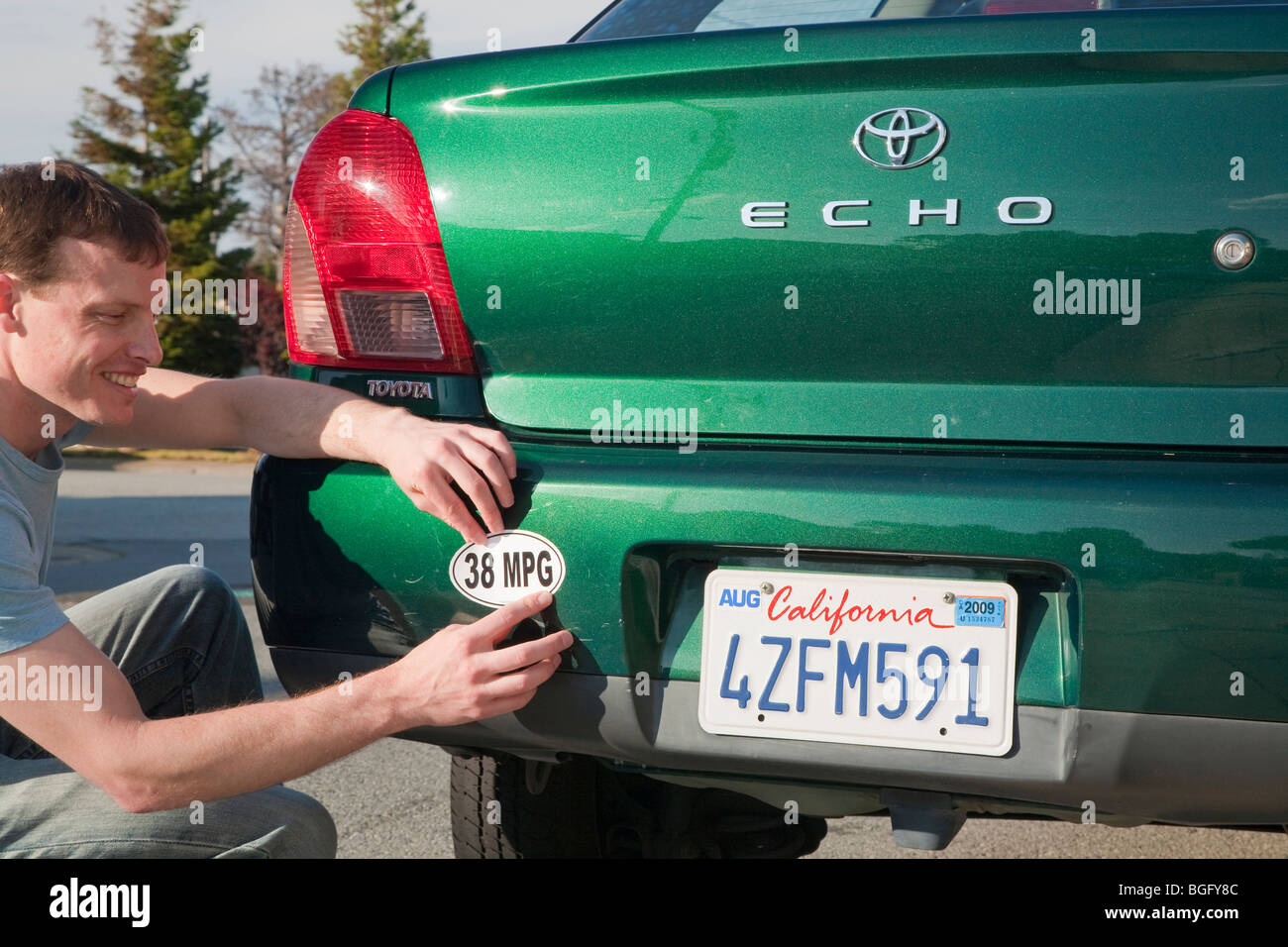 Man placing a 38 miles per gallon fuel efficiency bumper sticker ...