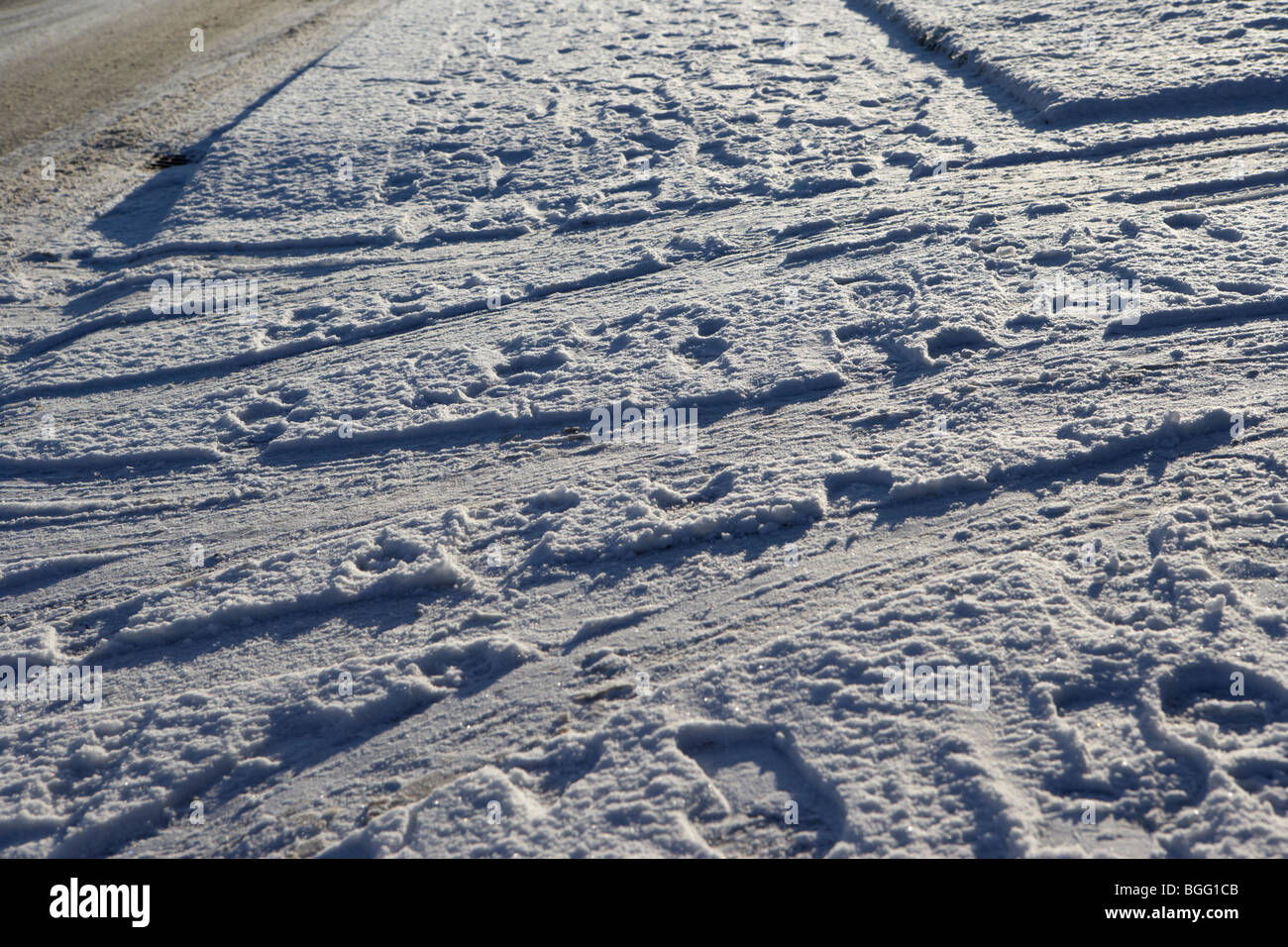 footprints and car tyre marks leaving a drive in the snow on a footpath ...
