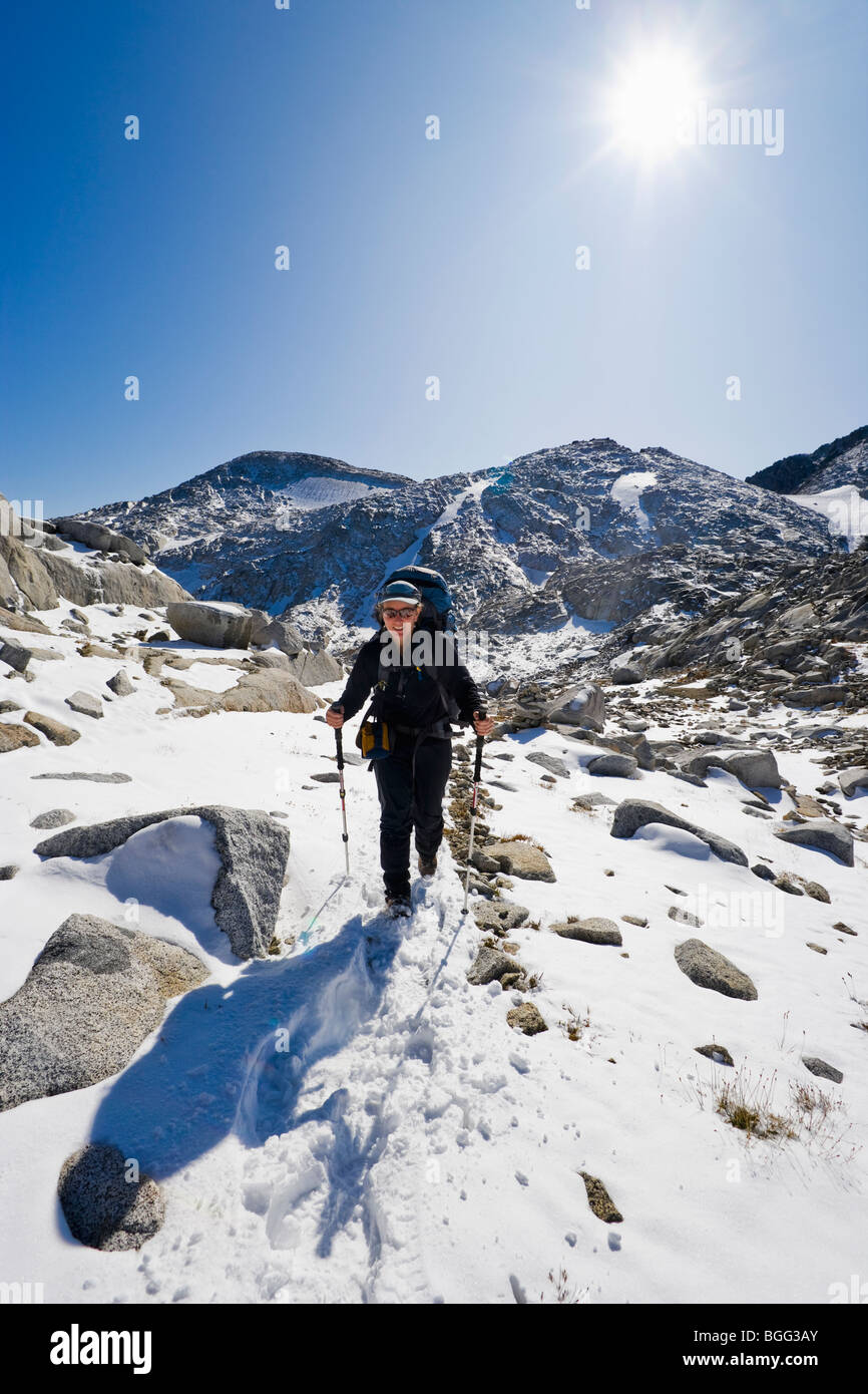 A woman wearing a backpack hiking in the snow through some high alpine ...
