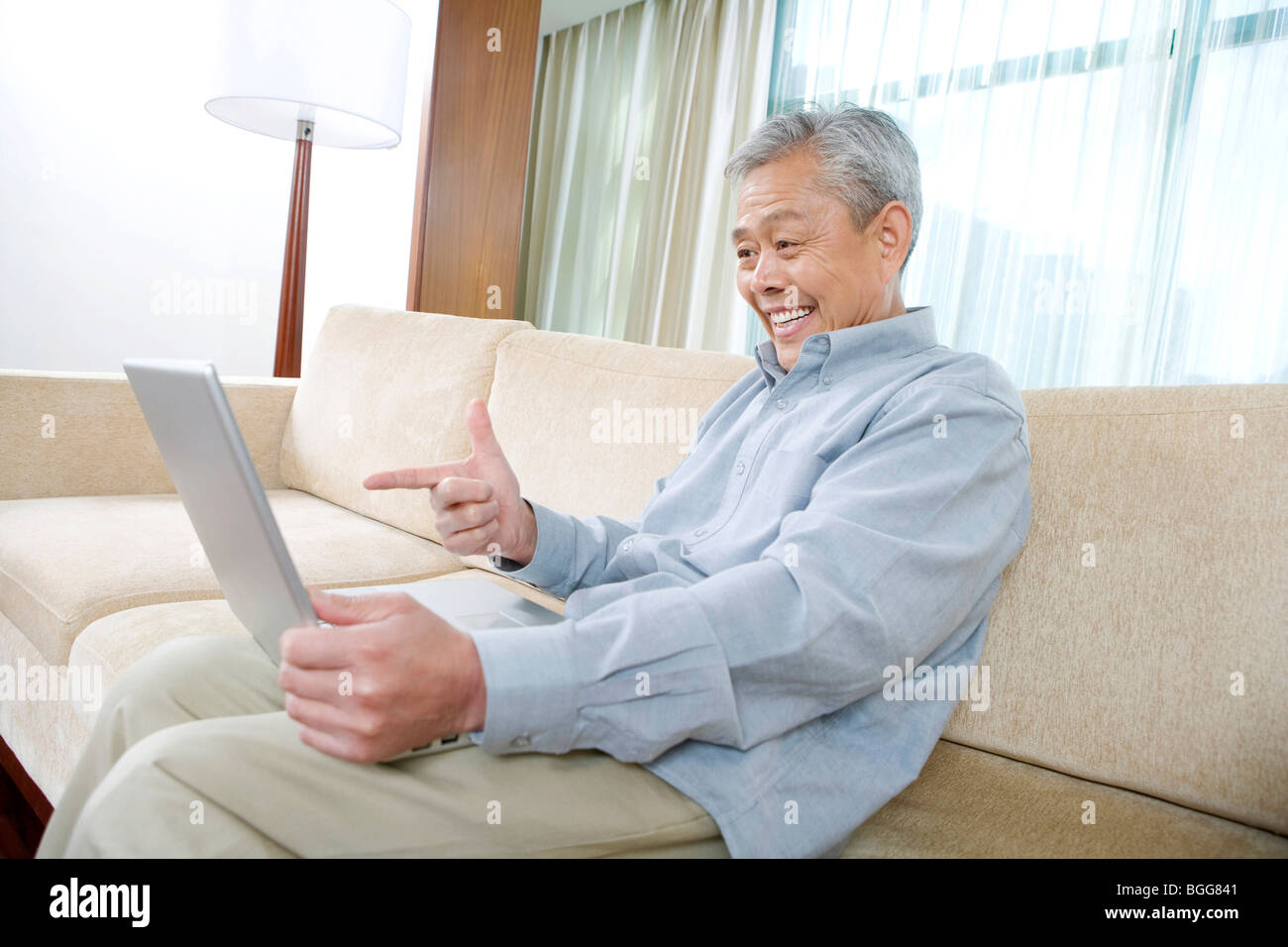 Smiling elderly man points at laptop screen on sofa Stock Photo - Alamy