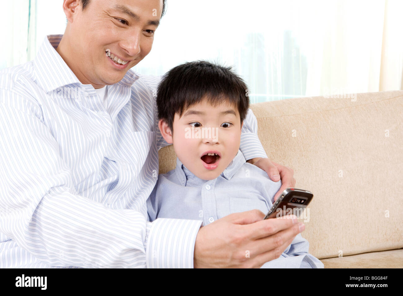 Father and son use cell phone or PDA on sofa Stock Photo - Alamy