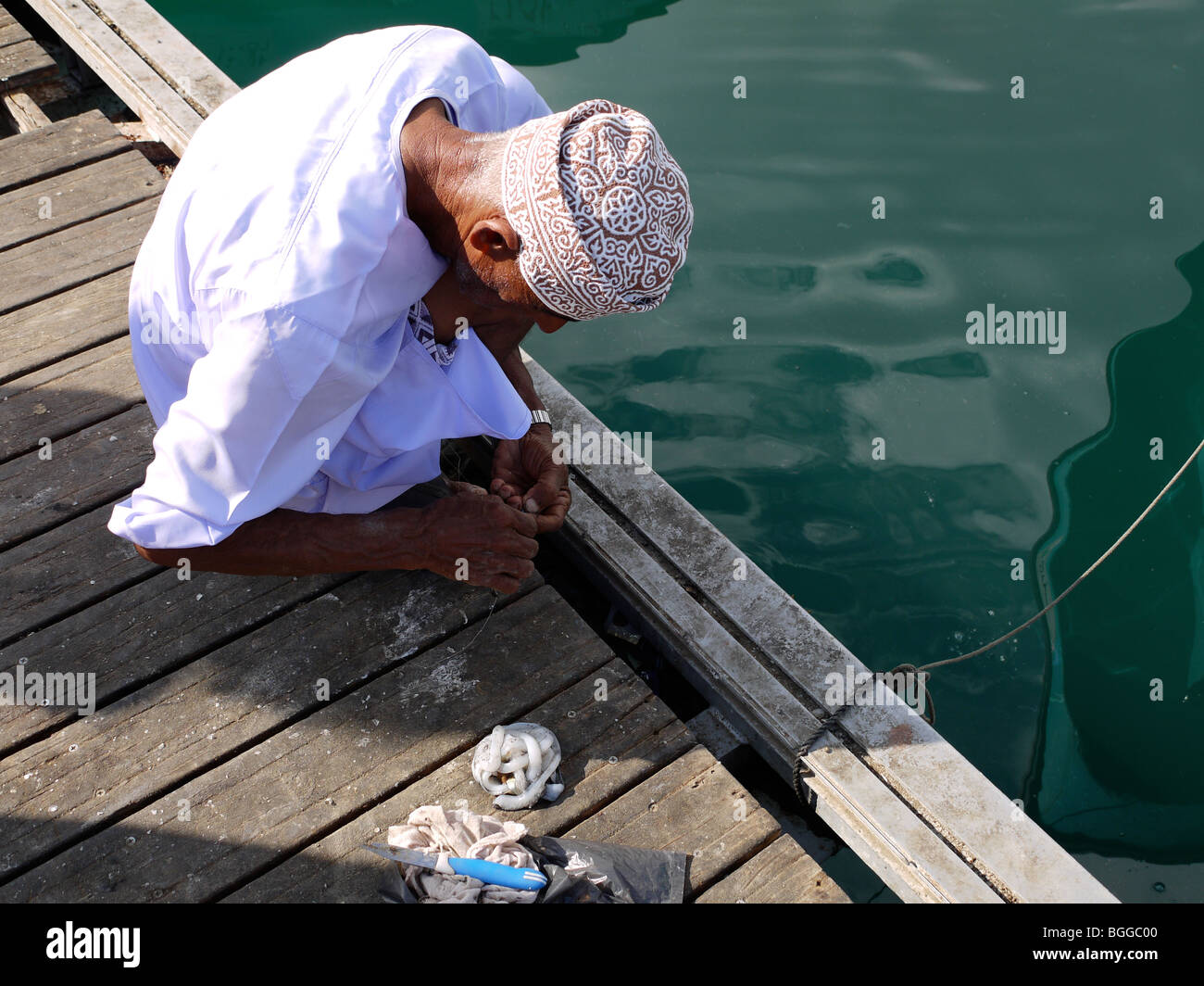 Omani man in traditional dress fishing from a pier near the Muscat fish ...