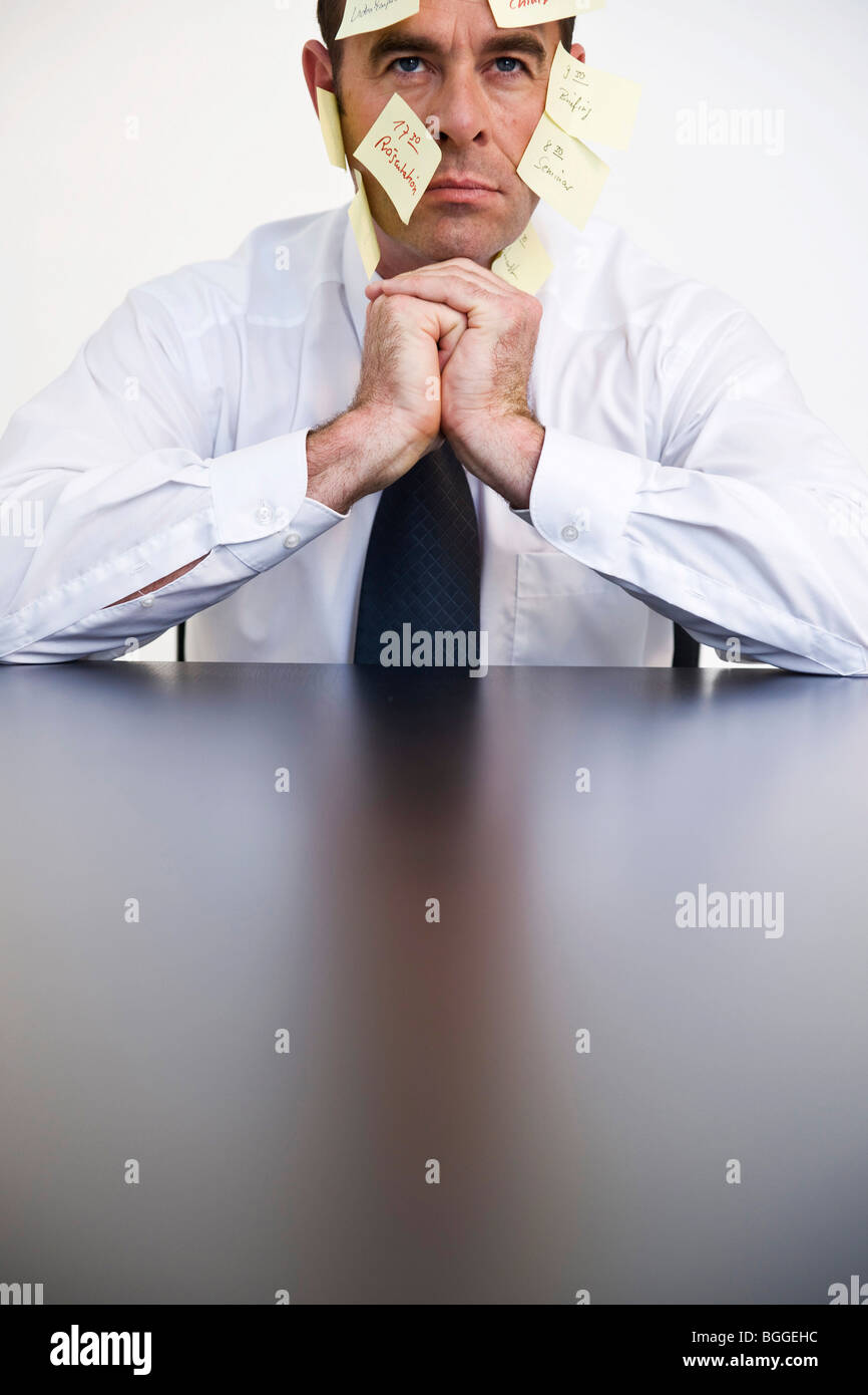 Businessman with post it notes at his face sitting at a table, front ...