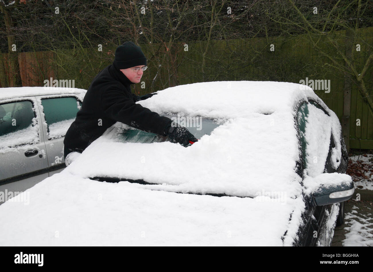 A cold man scrapping ice and snow from a car windscreen, in London, UK ...