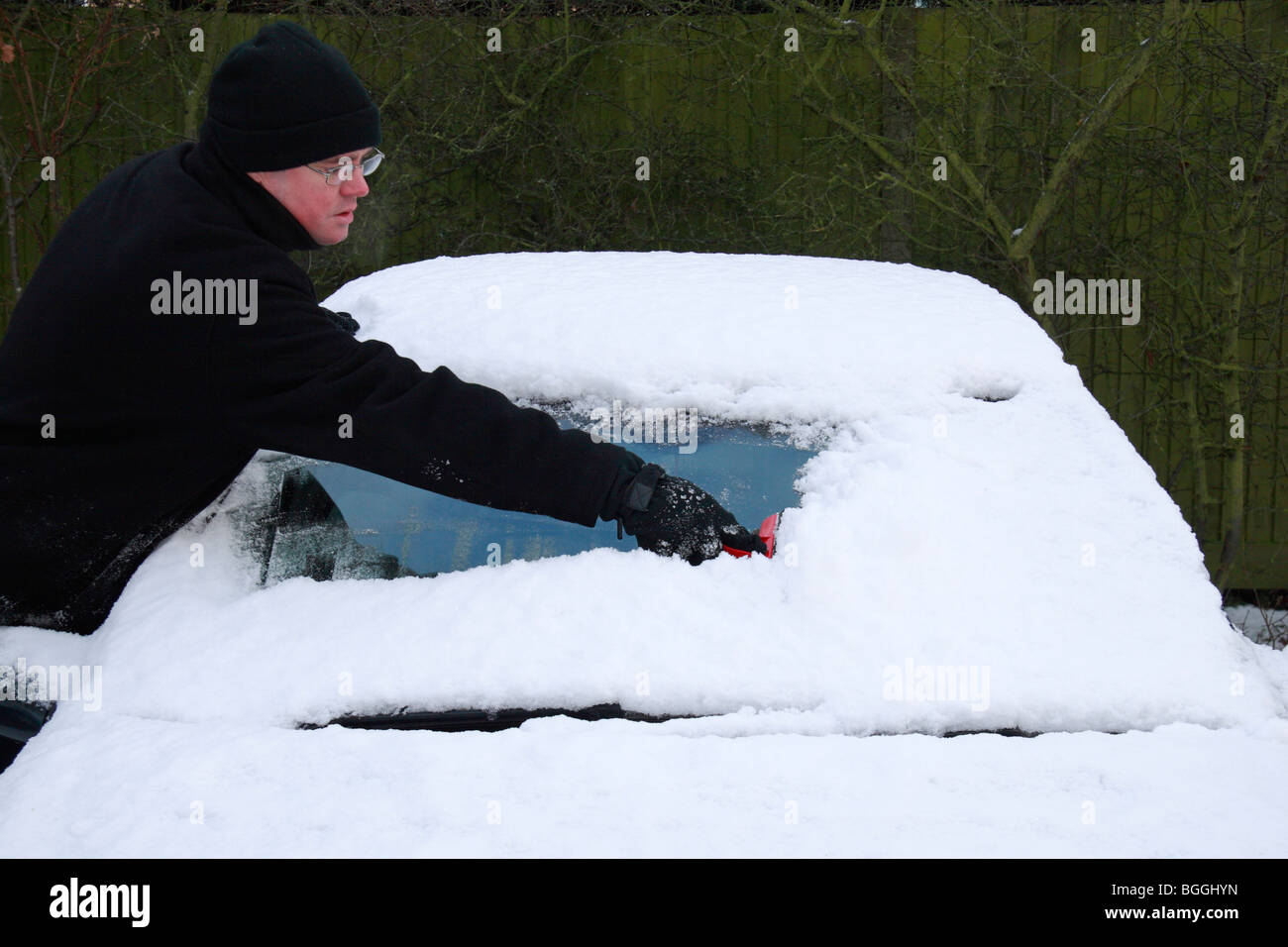 A cold man scrapping ice and snow from a car windscreen, in London, UK ...