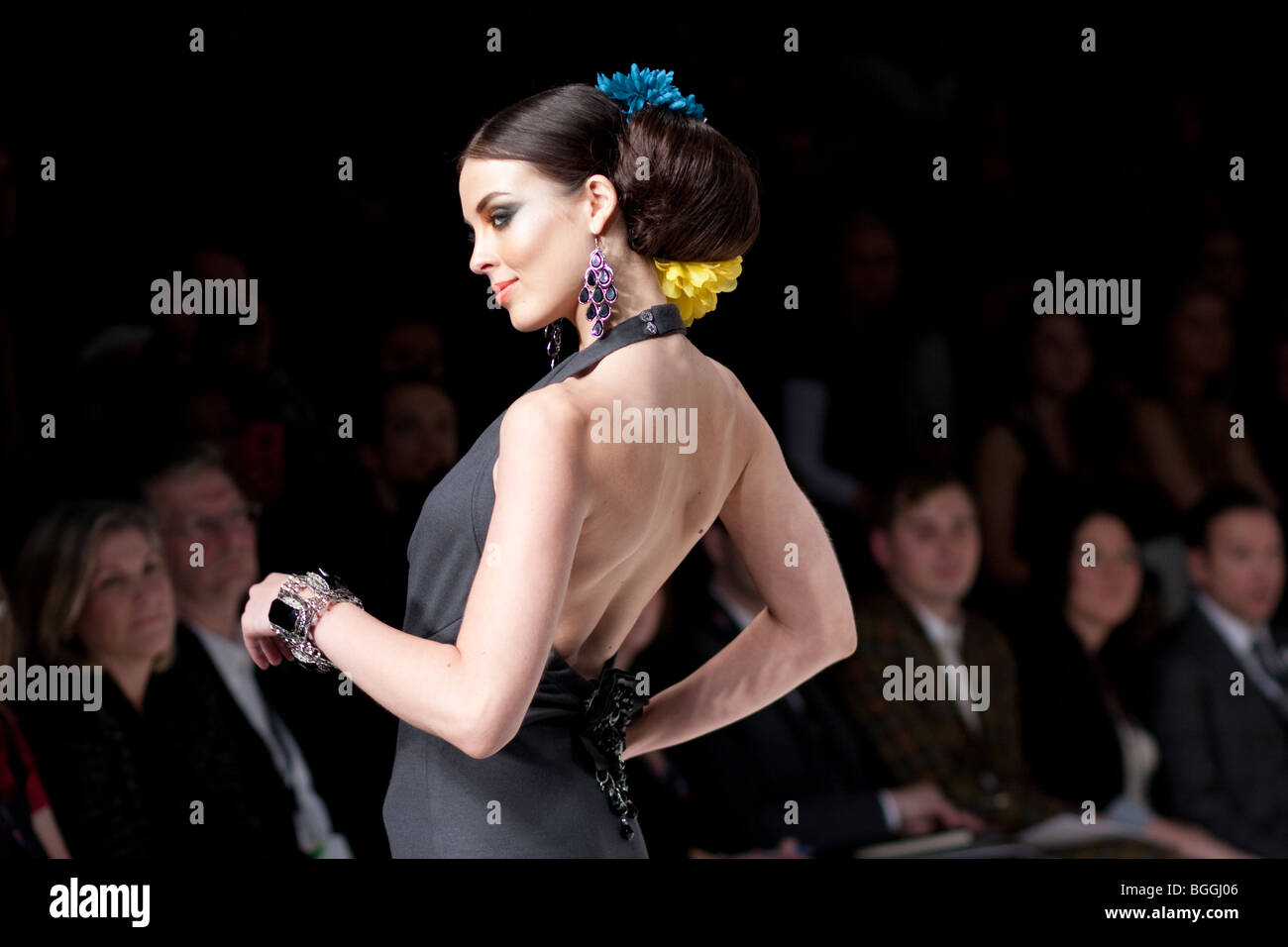 back of a model at a runway fashion show while audience are looking in ...