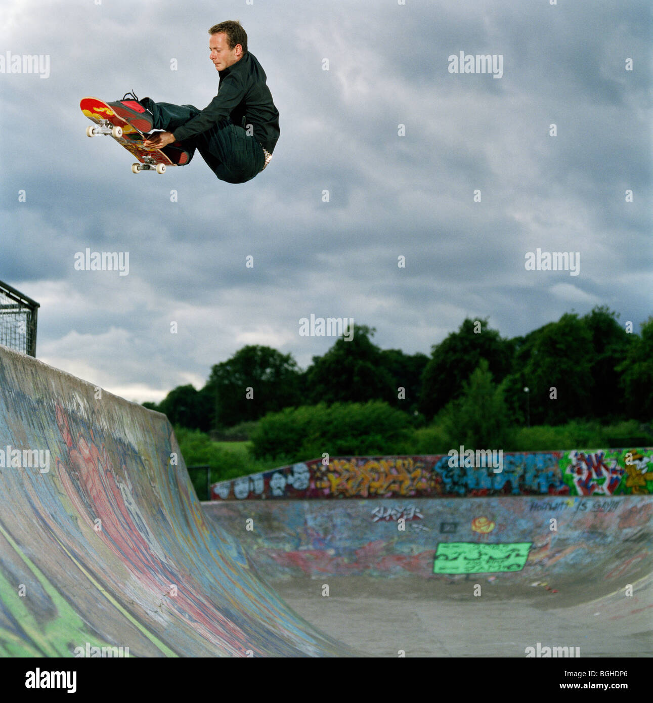 Skateboarder does an ollie grab at a graffitied outdoor skatepark Stock ...