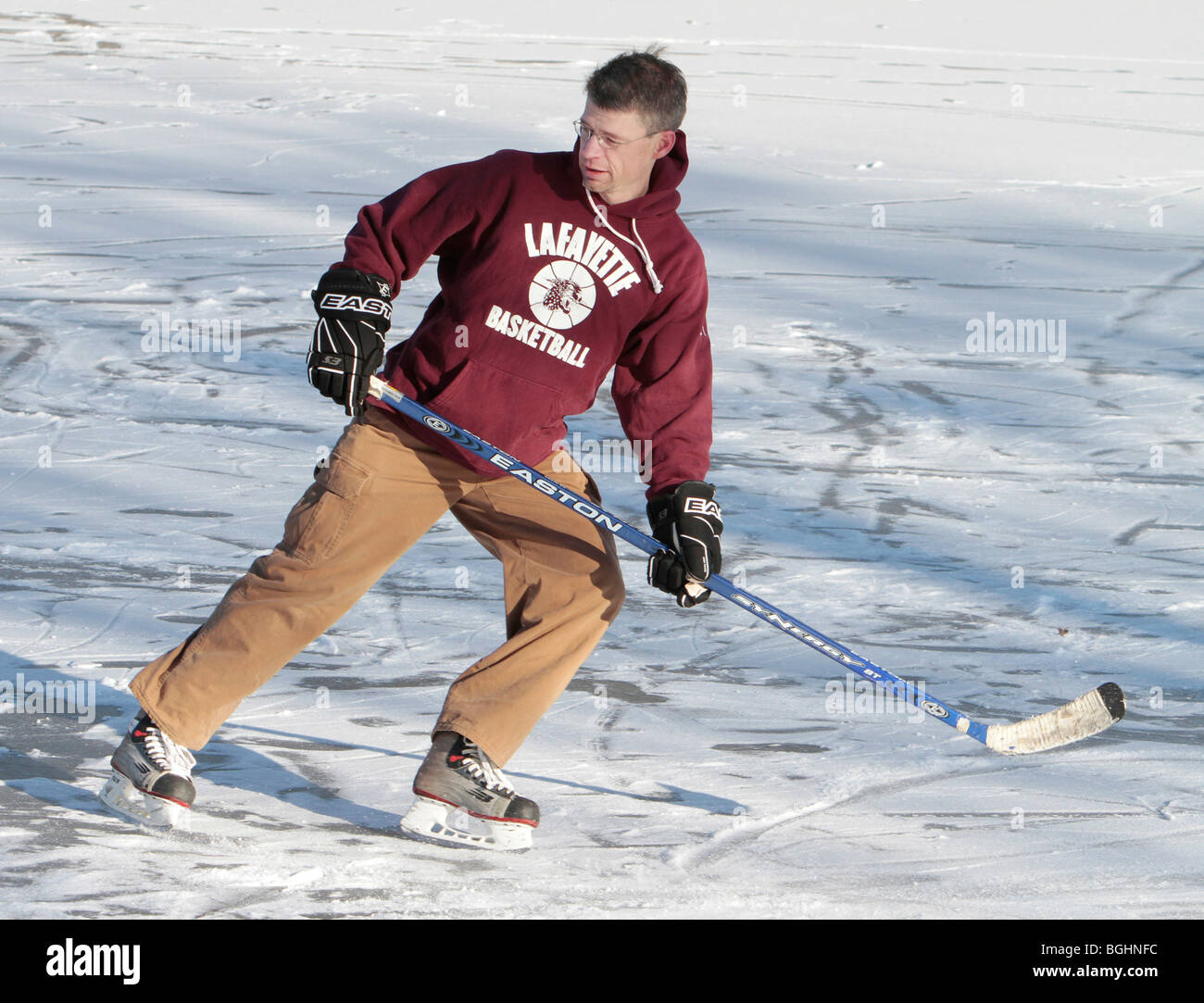 A young man ice skating. He is wearing hockey skates has a hockey stick ...