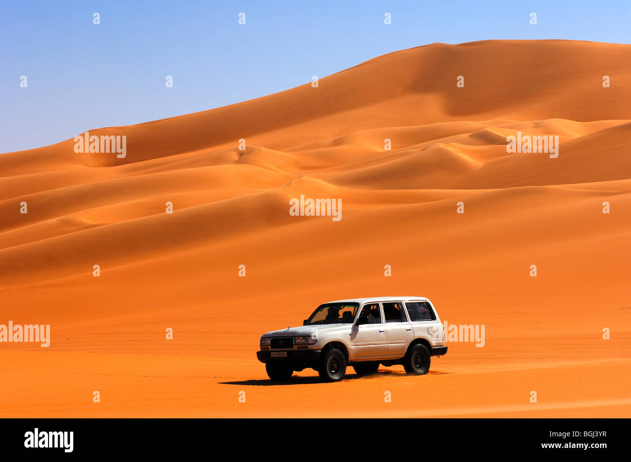 Four-wheel drive car driving in front of a mighty ochre sand dune in ...
