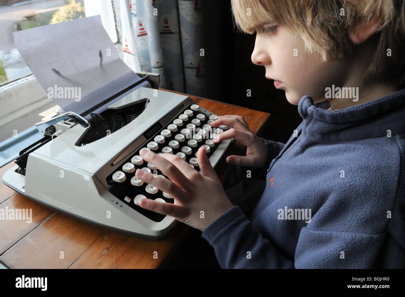Young boy typing a letter sitting at a desk with a typewriter, typing ...