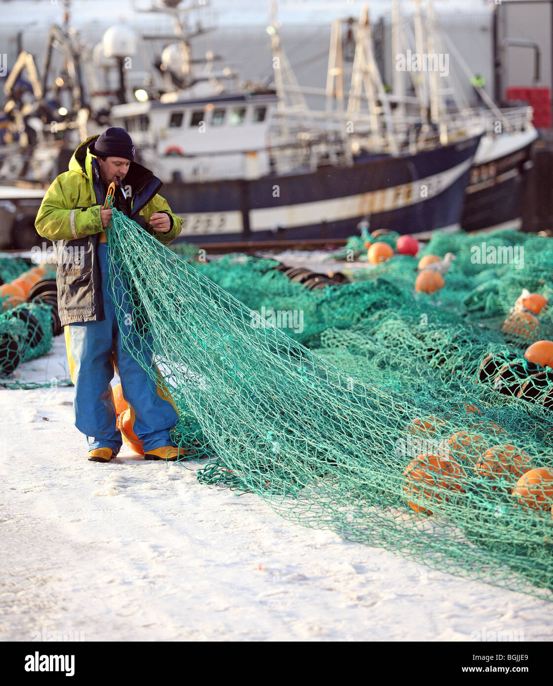 Fisherman wearing waterproof oilskins mending nets in the snow at the ...