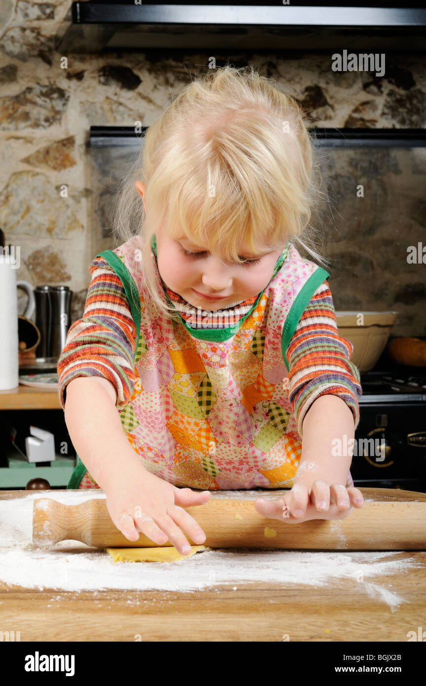 Stock photo of a four year old girl using a rolling pin to flatten the ...