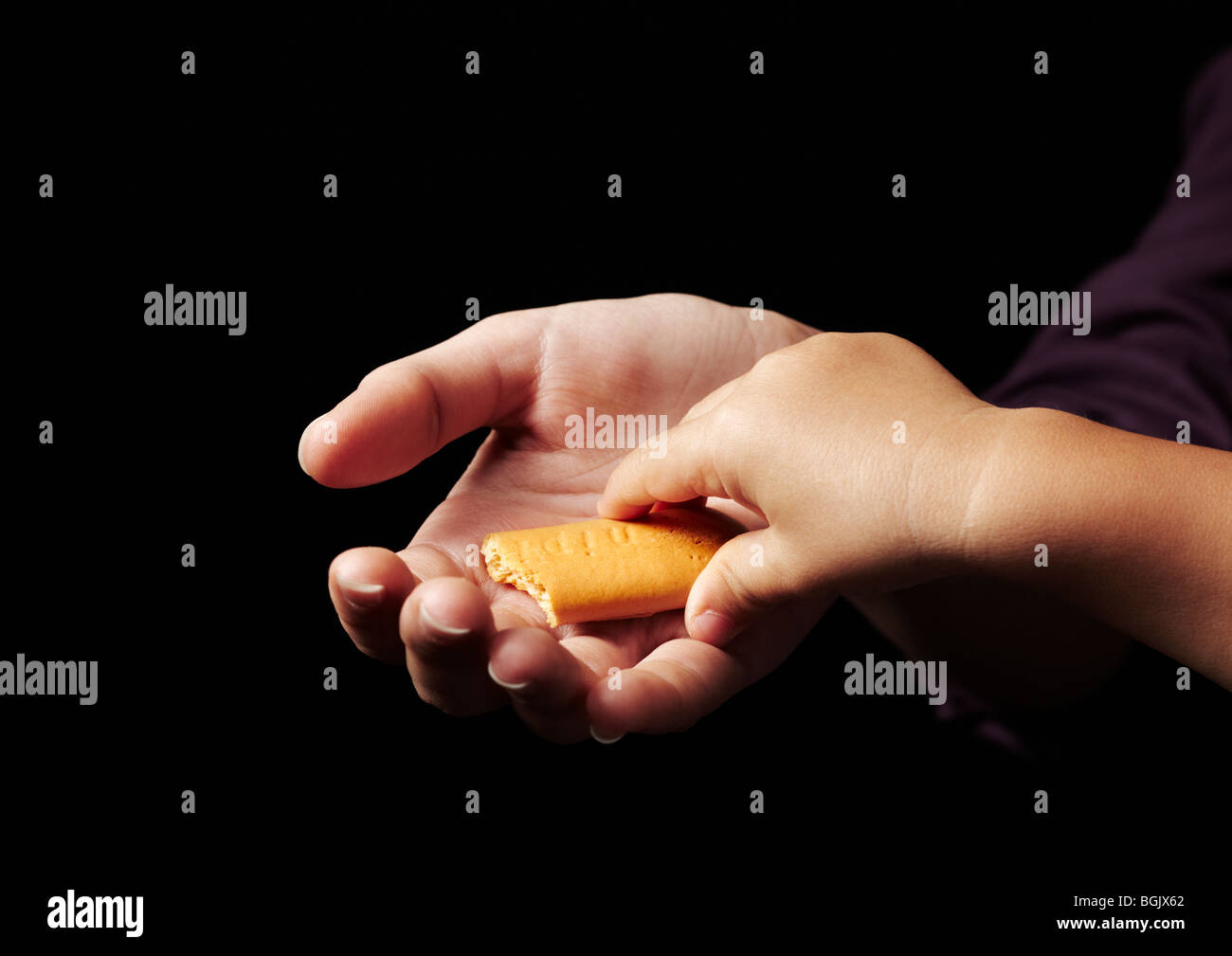 Woman hand holding a biscuit on dark background with child hand ...