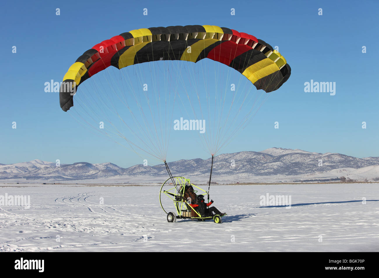 Powered parachute aircraft flying from a frozen lake near mountains ...