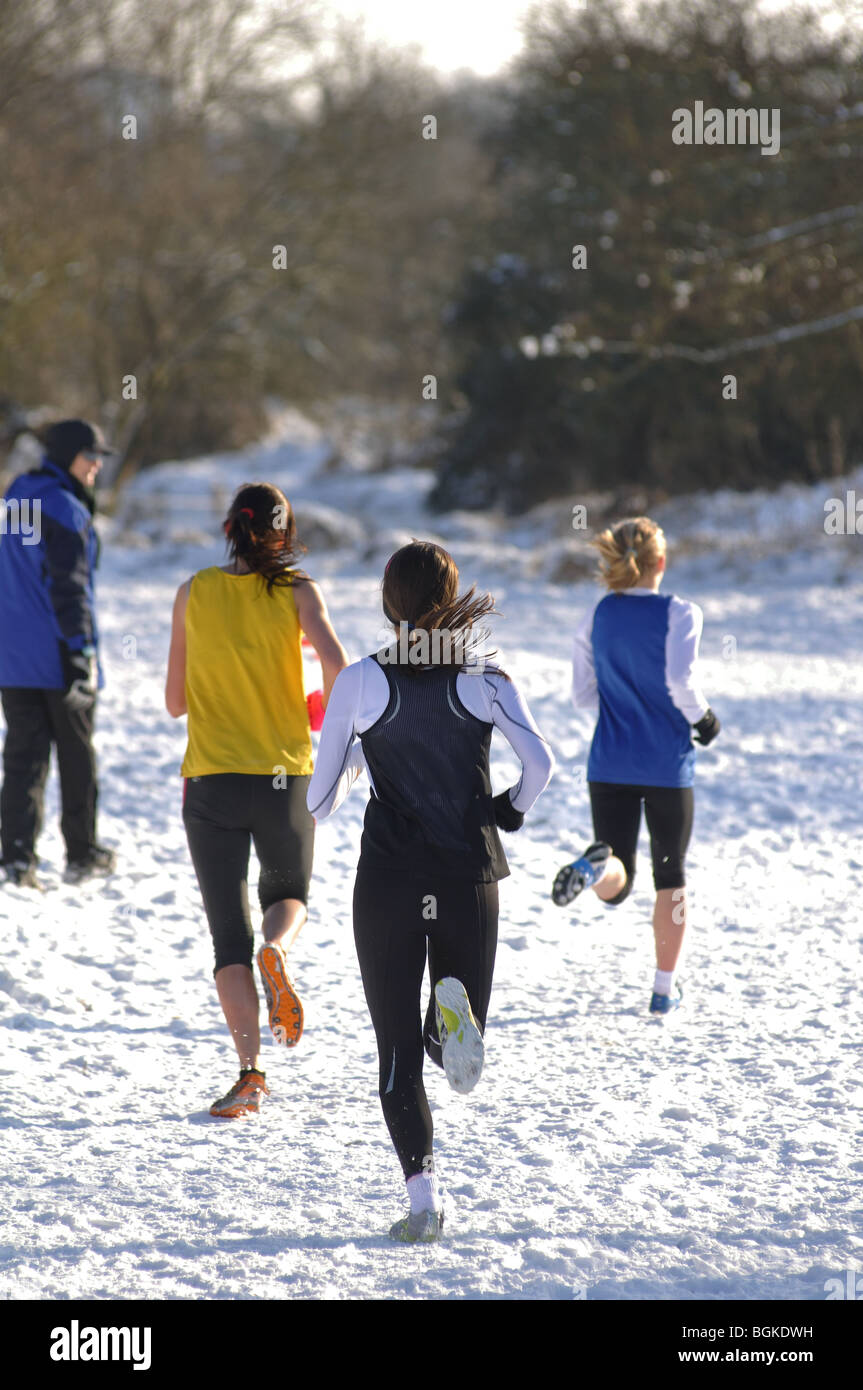 Teenage girls running in cross-country race in snow seen from behind ...