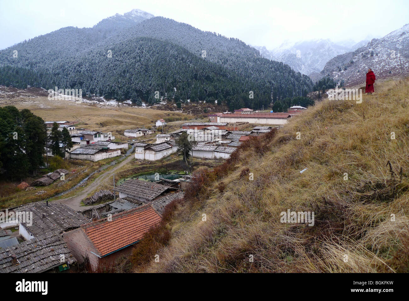 Monk in red robes standing in front of the village and the Tibetan ...
