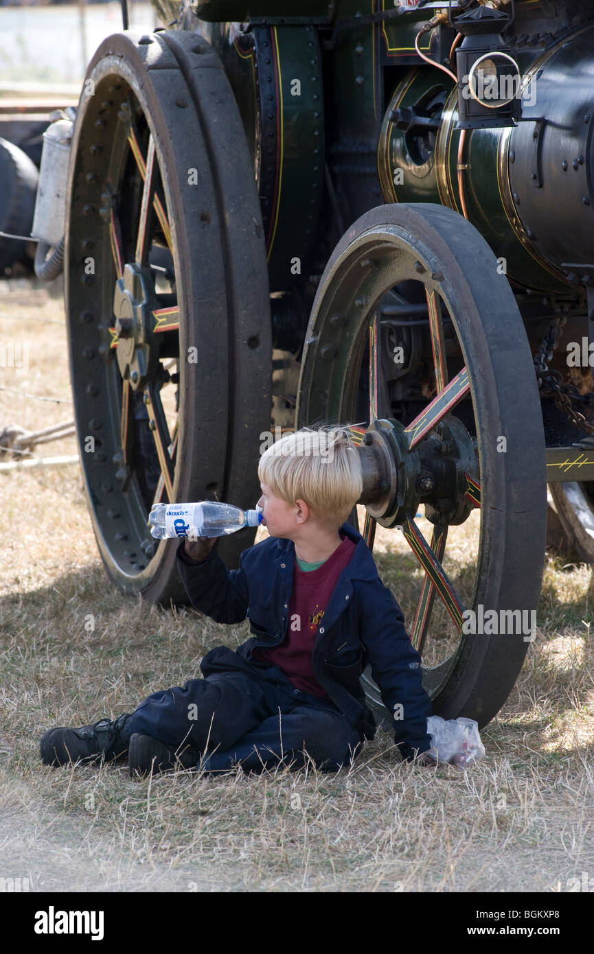 small boy in overalls drinking bottled water sitting in front of ...