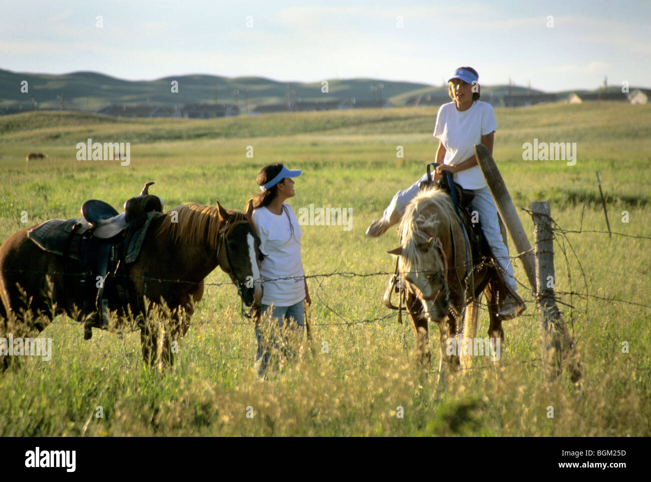 Two Blackfeet teenage girls ride horses in a field with a barbed wire ...