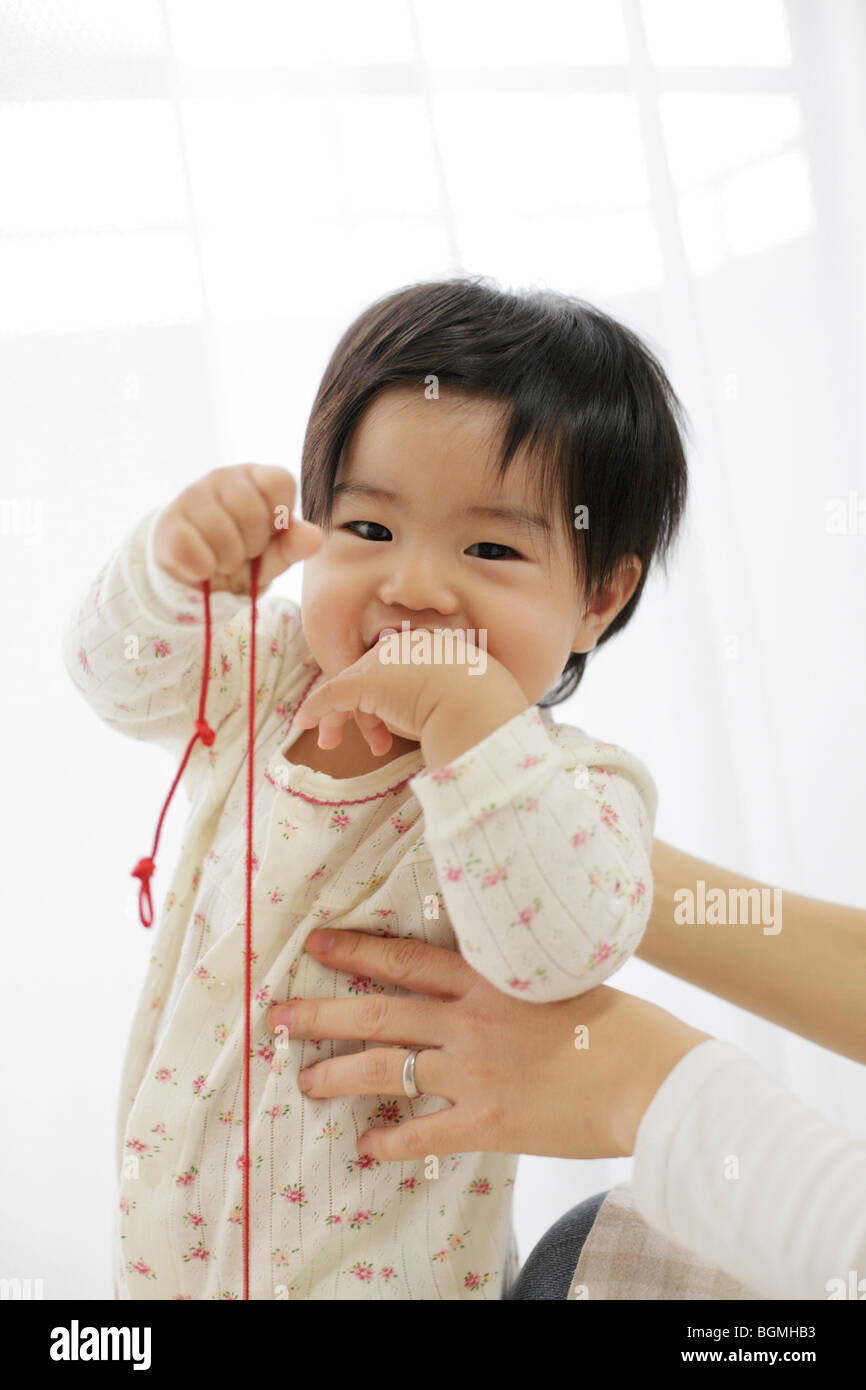Baby holding string and covering mouth with hand Stock Photo - Alamy