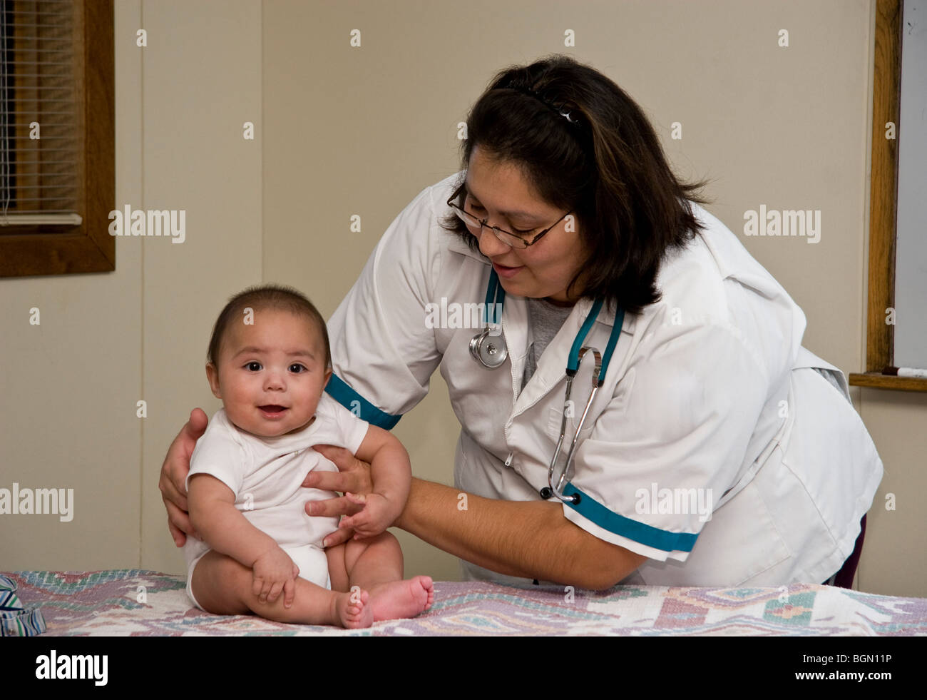 Native American nurse looks over the health of happy infant during a ...