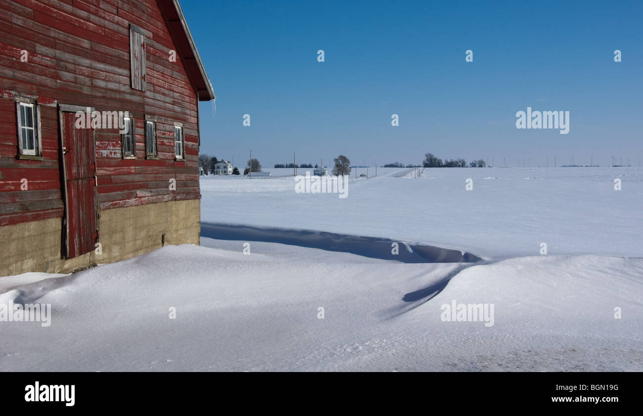 A small snowdrift pools around an old red barn on the frozen prairie ...