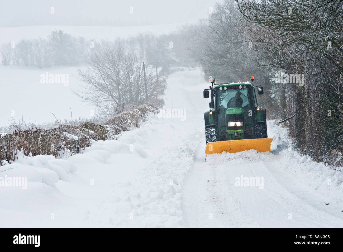 A farmer driving a tractor fitted with a snowplough attempts to clear ...
