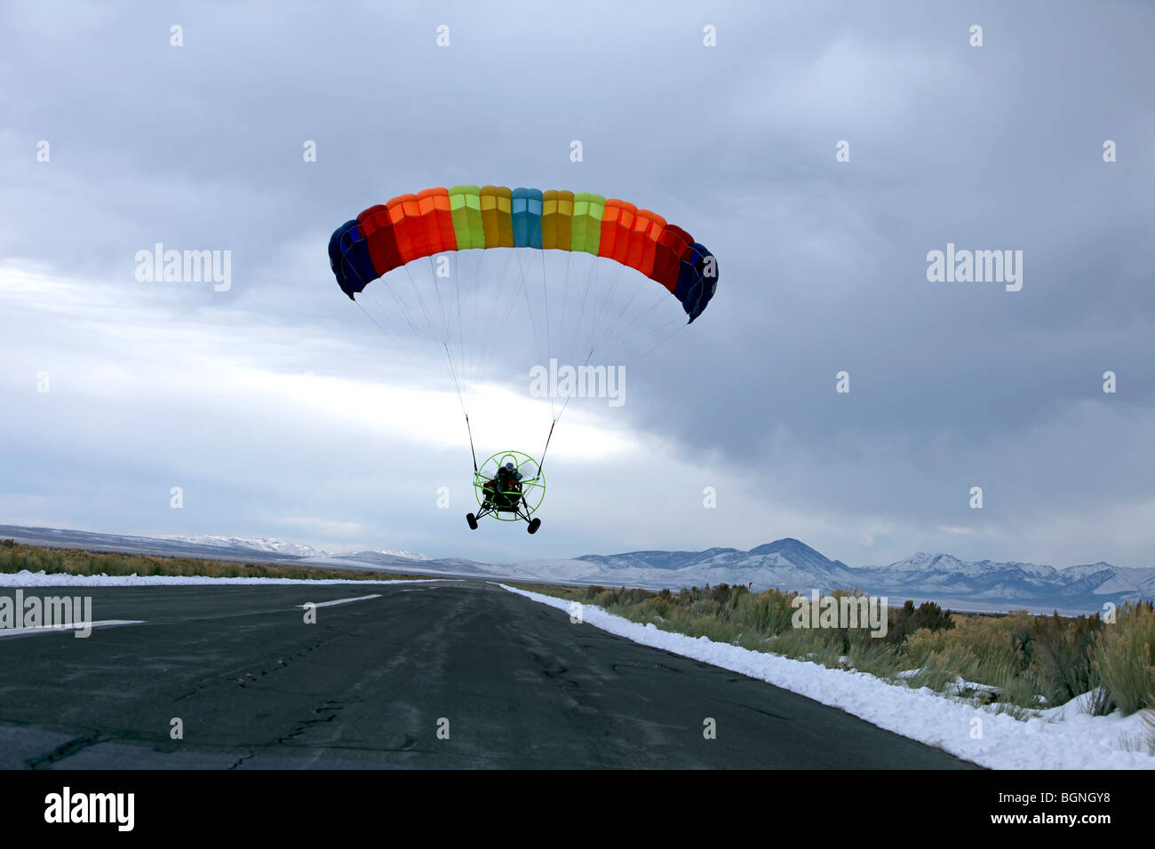 Powered parachute flying low over runway with snow covered mountains ...
