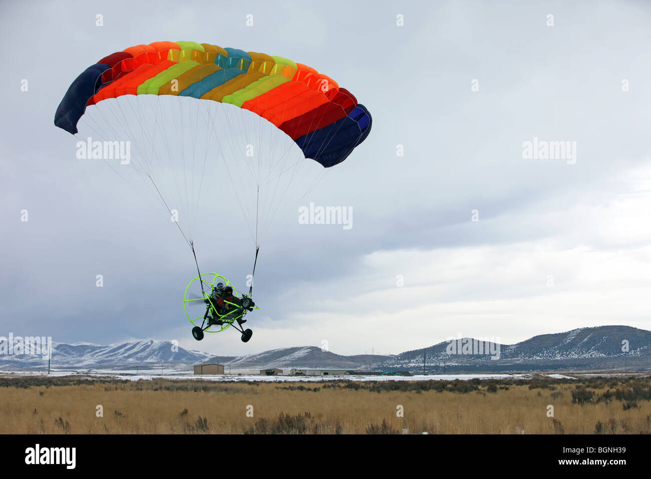 Powered parachute flying low over dry field with snow covered mountains ...