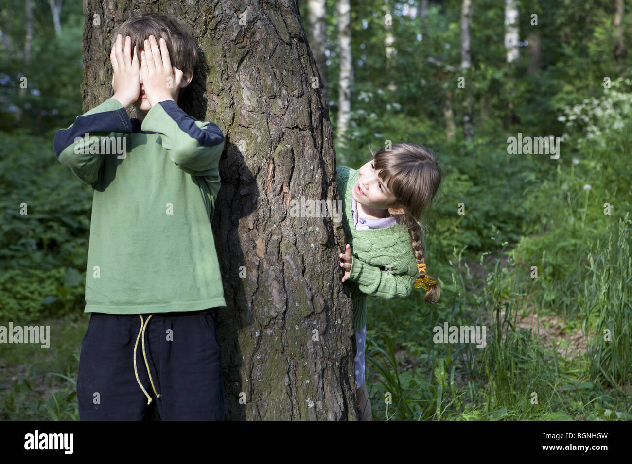boy close his eyes by hand. Girl look out tree. Hide-and-seek Stock ...