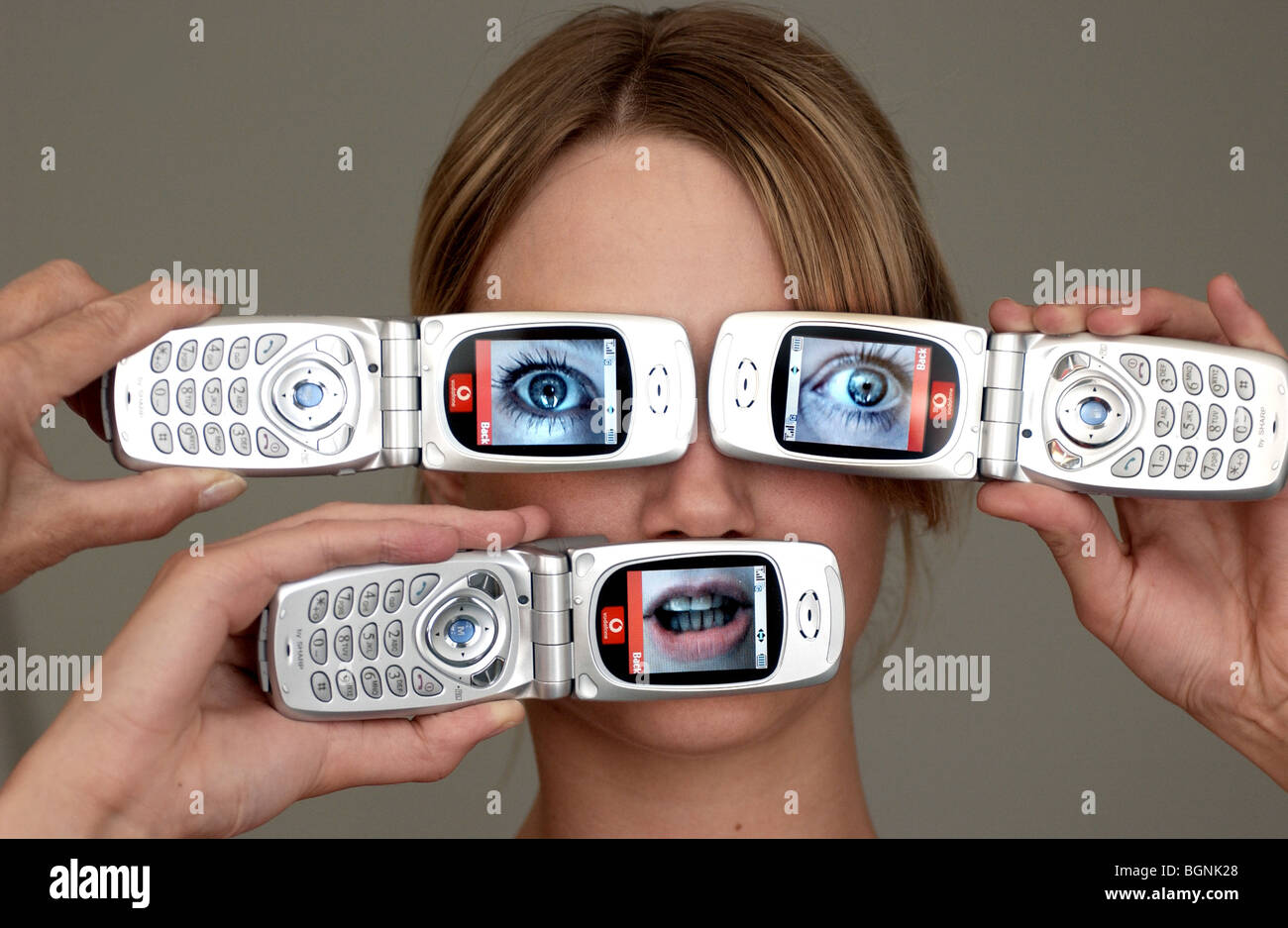 A girl playing with three mobile camera phones with images of big eyes ...