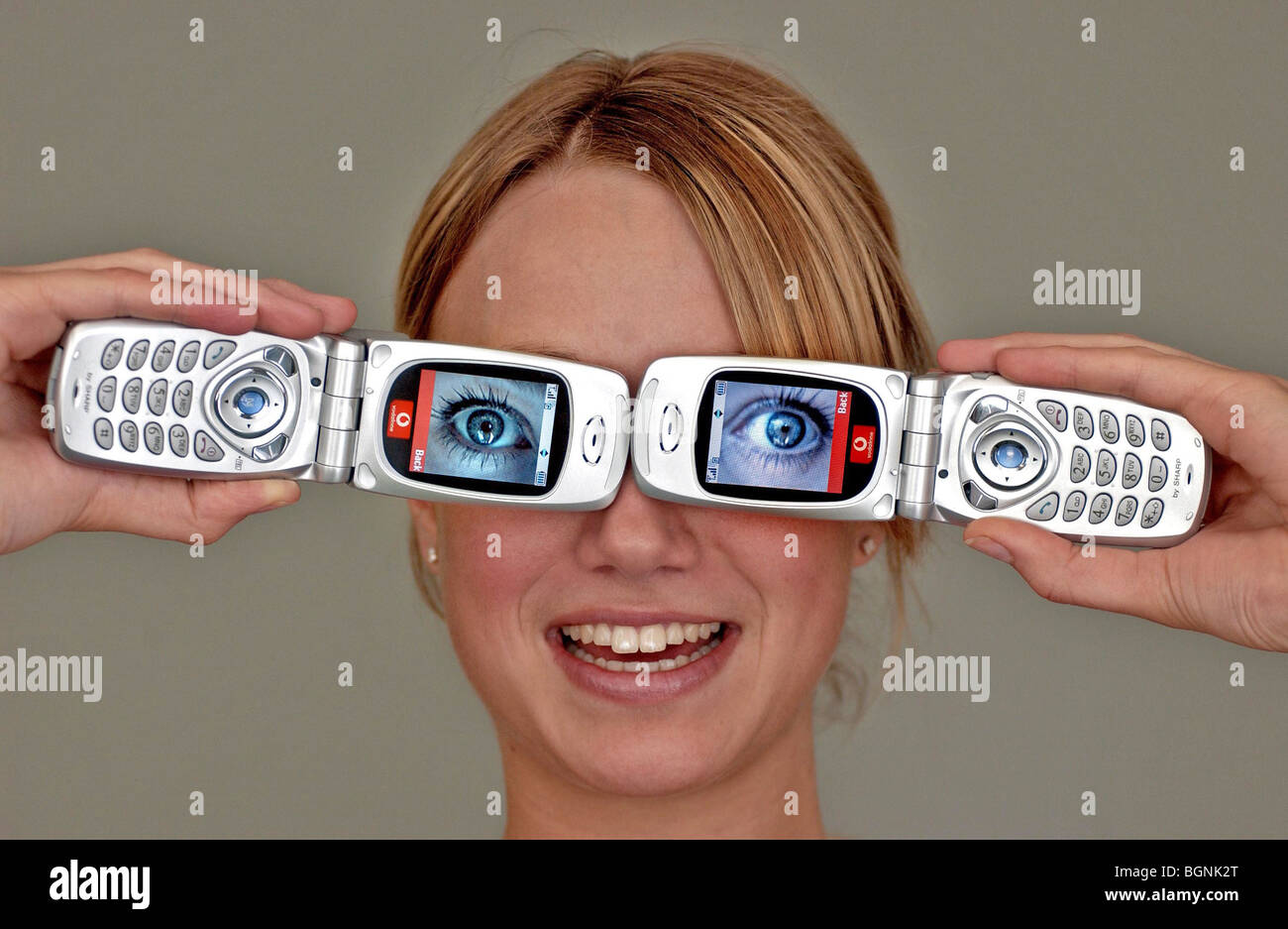 A pretty smiling girl playing with two mobile camera phones with images ...