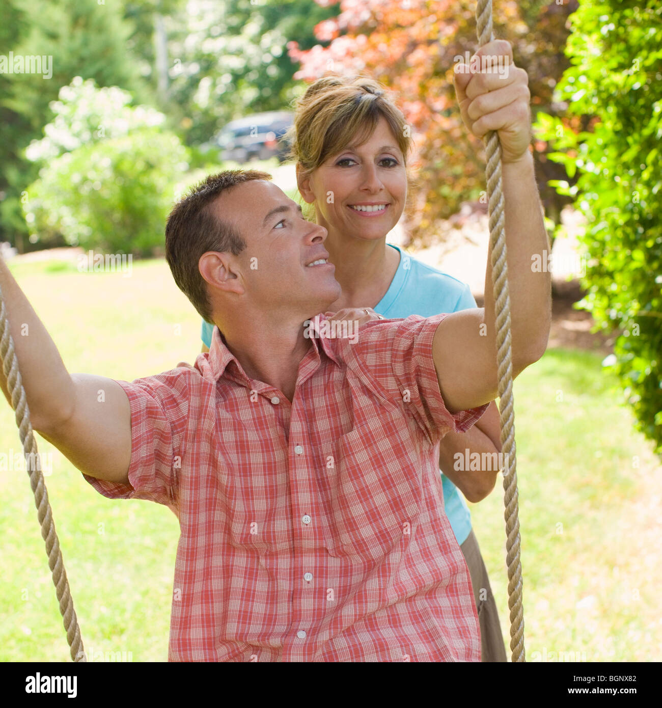 Mature woman pushing a mature man on a rope swing and smiling Stock ...