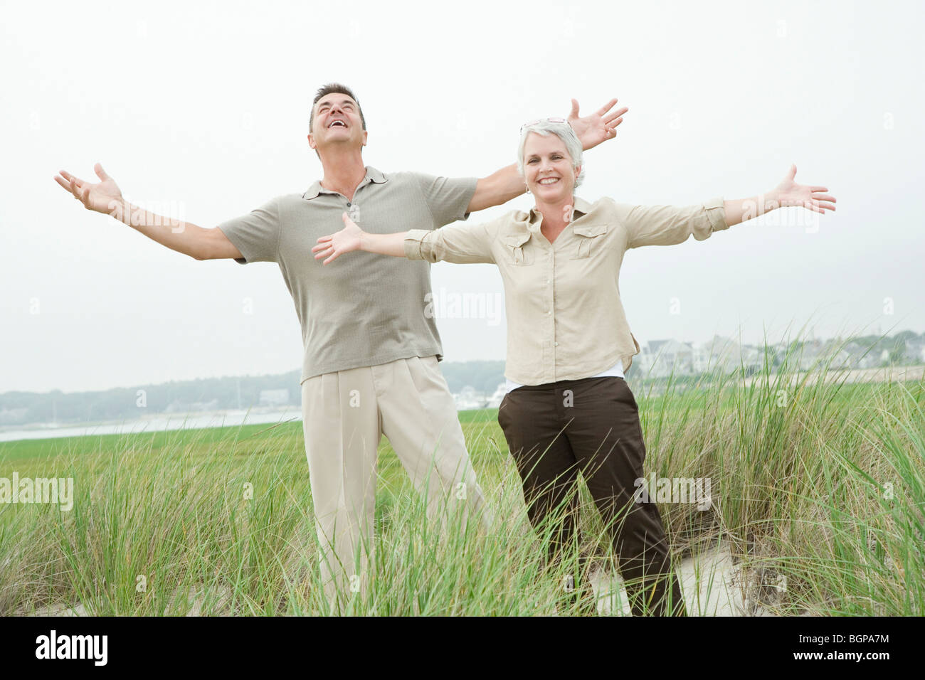 Mature couple standing with their arm outstretched in a grassy field ...