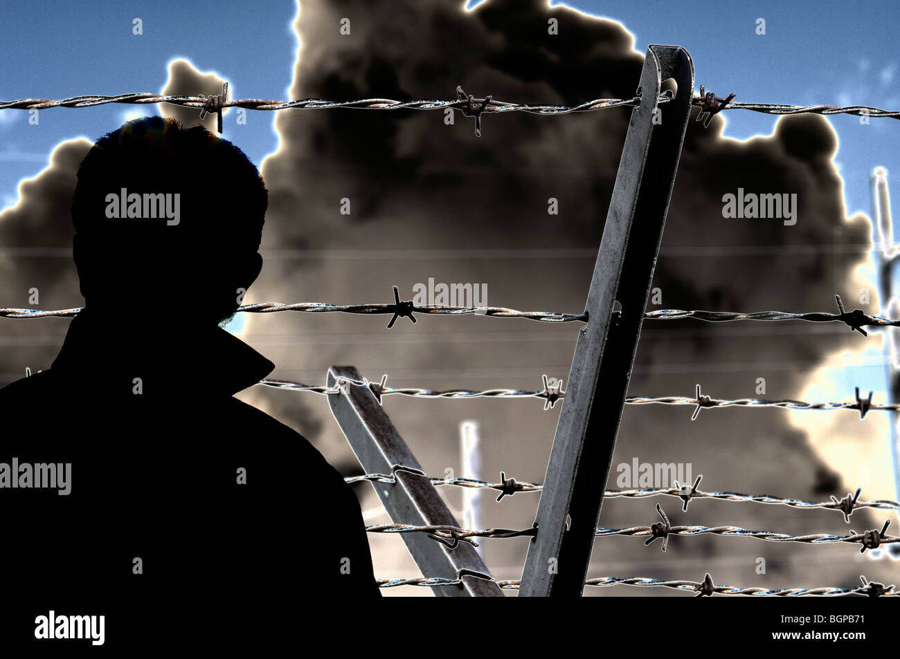 man behind barb wire fence silhouetted against stormy sky at sunset in ...