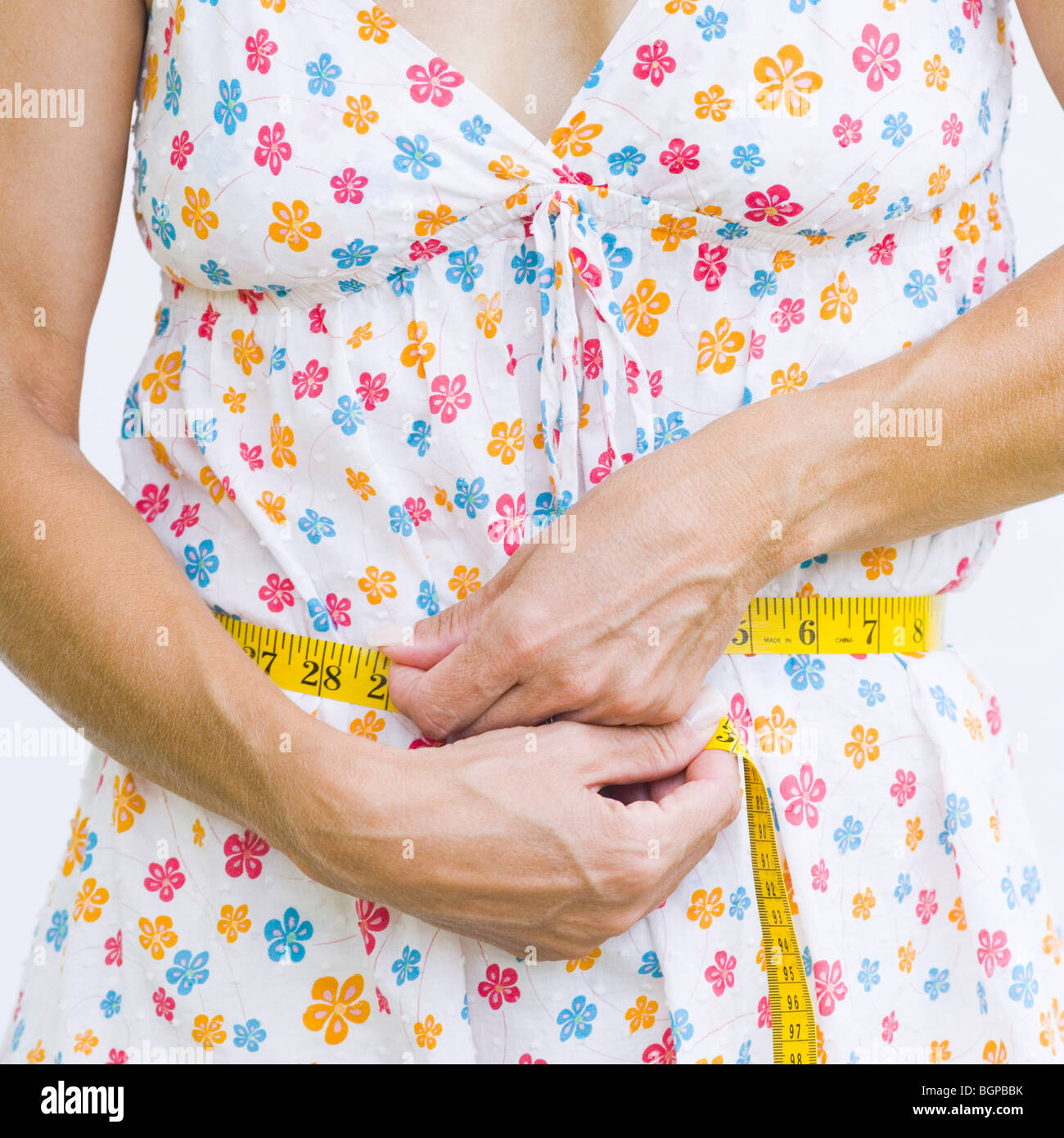 Mid section view of a woman measuring her waist with a tape measure ...