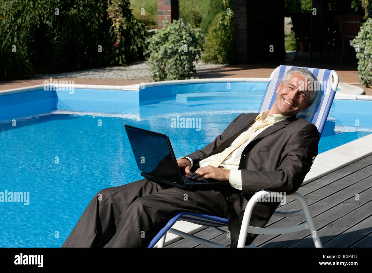 Happy businessman sitting on deck chair with laptop computer next to ...