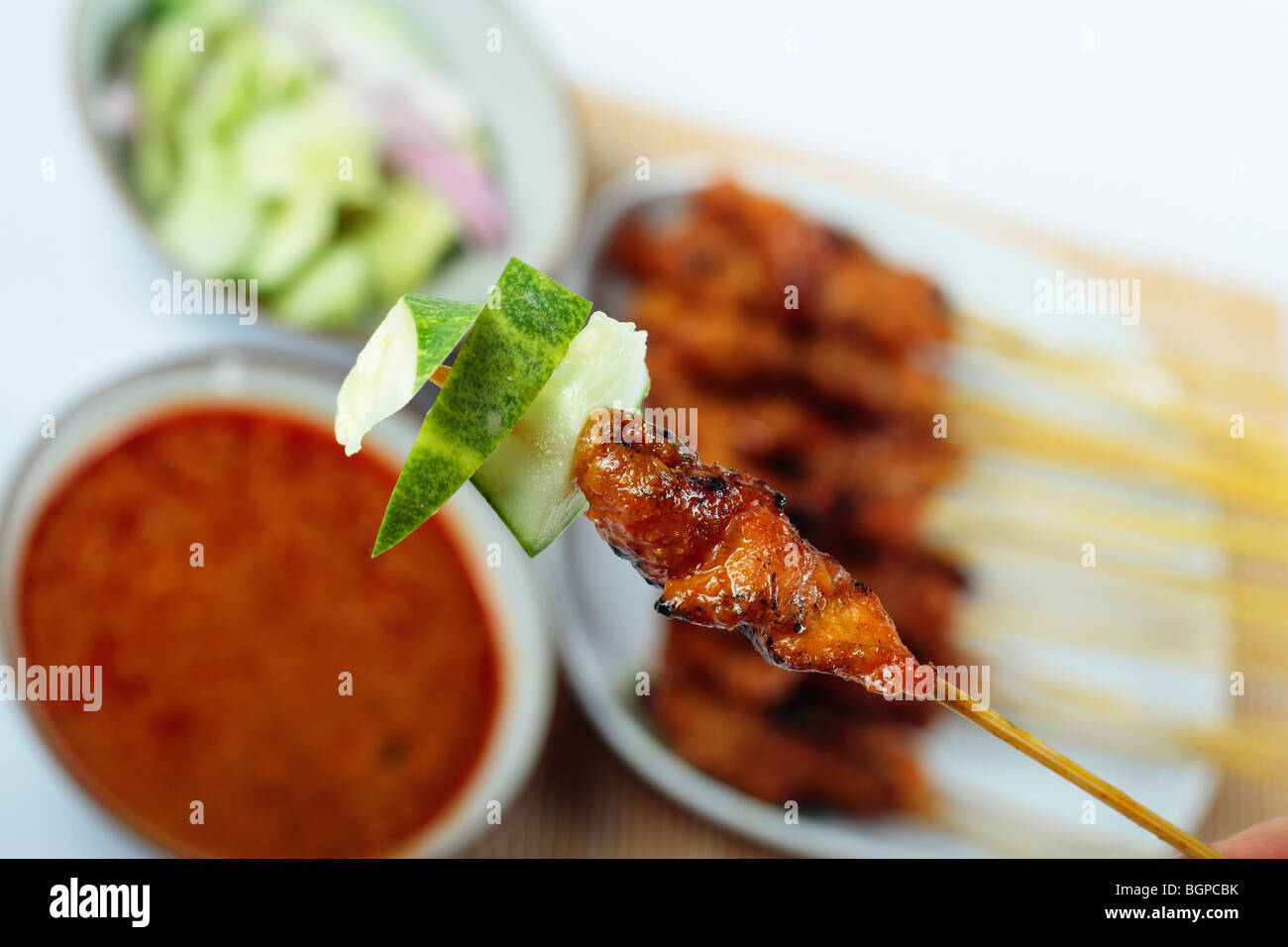 A stick of chicken satay and sliced cucumber with peanut gravy, sliced ...