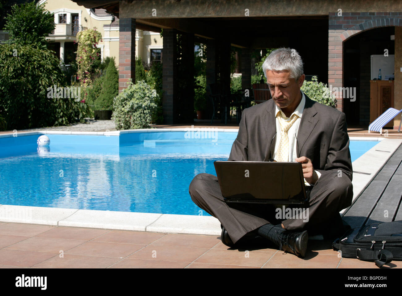 Handsome businessman sitting next to swimming pool with legs crossed ...