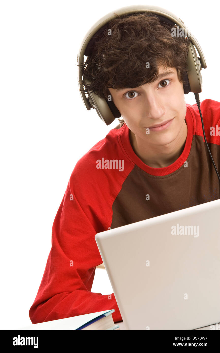 Teenage boy sitting behind desk with laptop computer listening to music ...