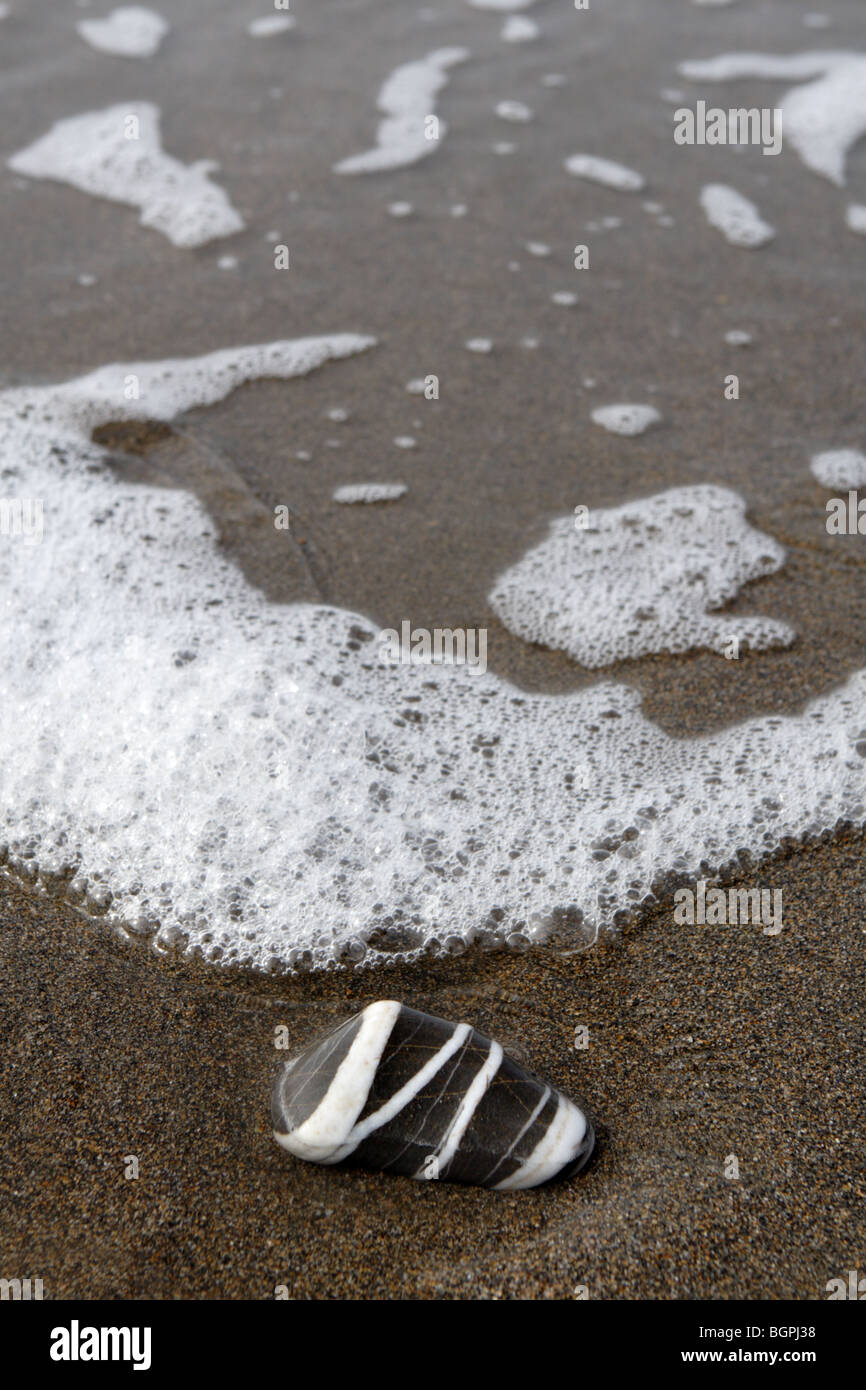 A stripy white and grey pebble sits in the sand on a north cornwall ...