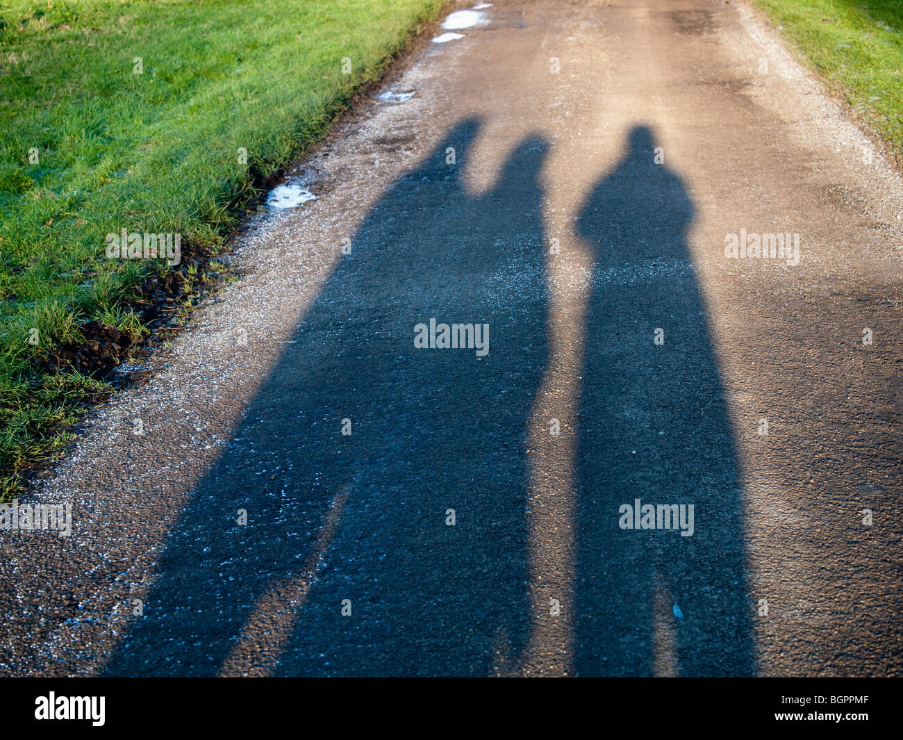the shadows of three people walking down a road Stock Photo - Alamy