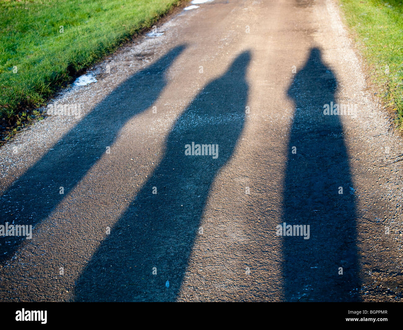 the shadows of three people walking down a road Stock Photo - Alamy
