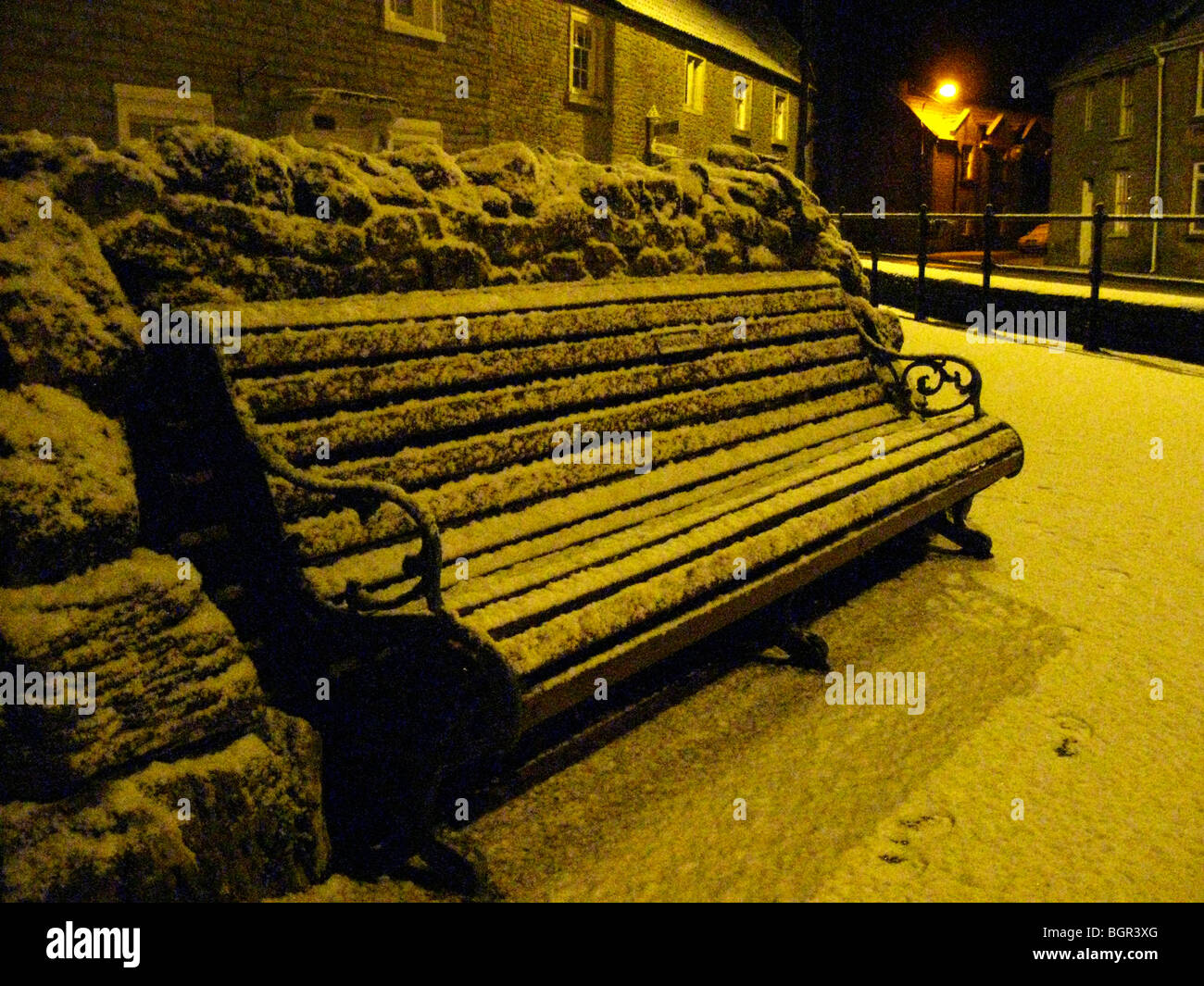 A wooden park bench at night covered in light dusting of snow, with ...