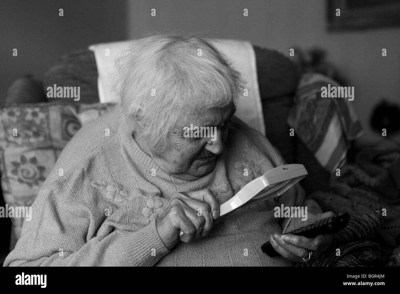 Old lady trying to understand technology, looking at her TV remote with ...