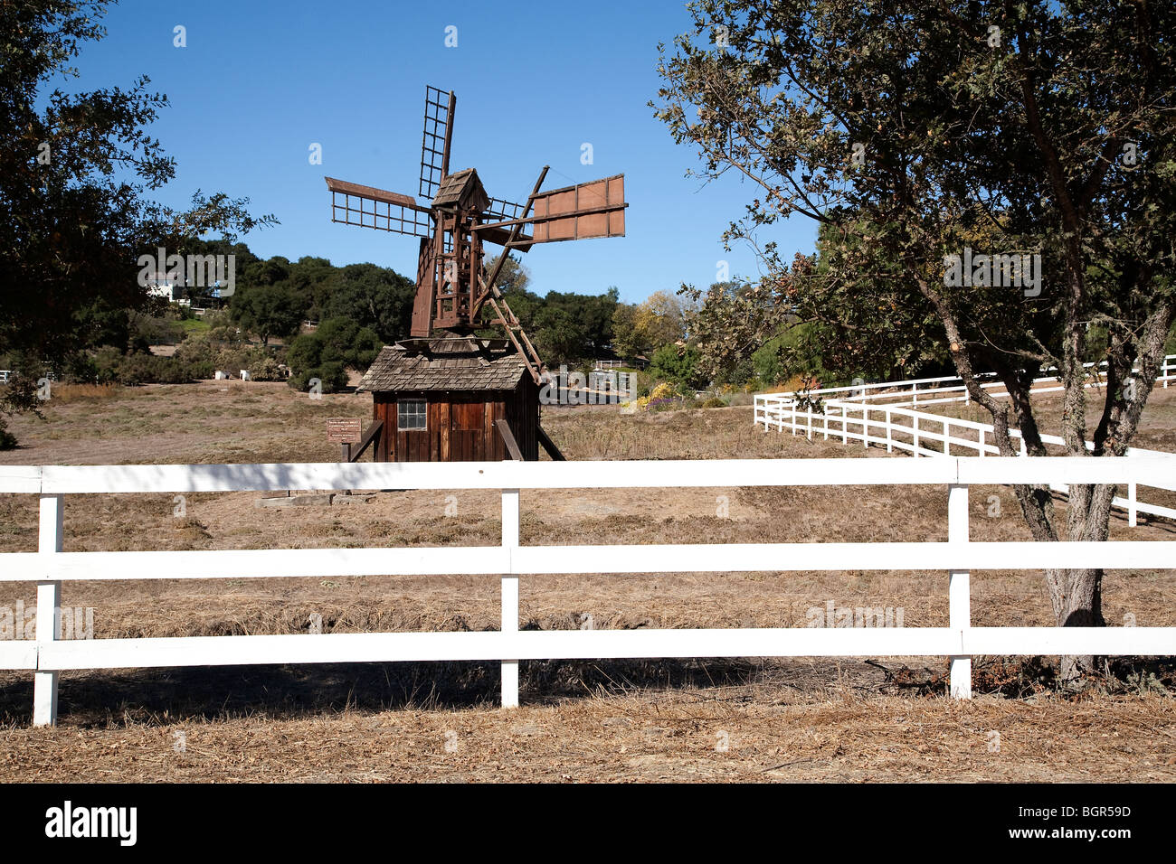 An old wooden windmill sits behind a white rail fence in the Santa Ynez ...