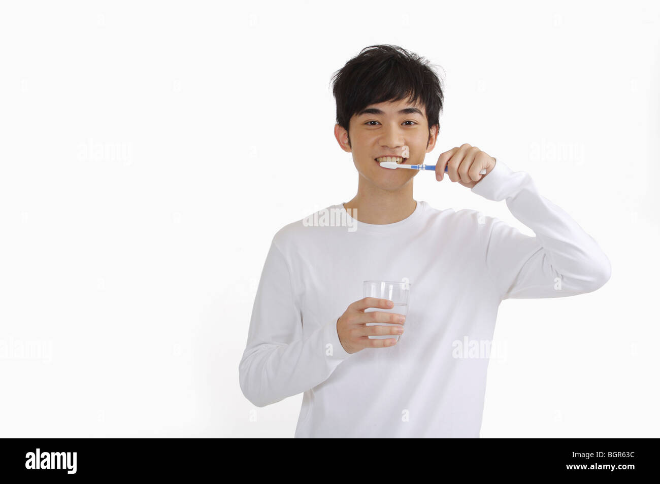 Young man holding a cup and brushing teeth Stock Photo - Alamy