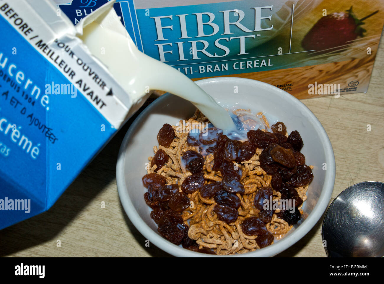 Pouring skim milk over healthy high fiber bran breakfast cereal raisins ...