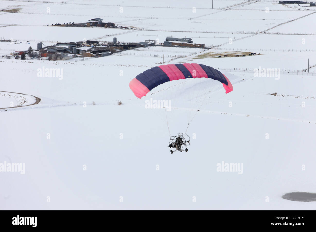 Powered parachute flying over ice and snow valley during winter. Farms ...