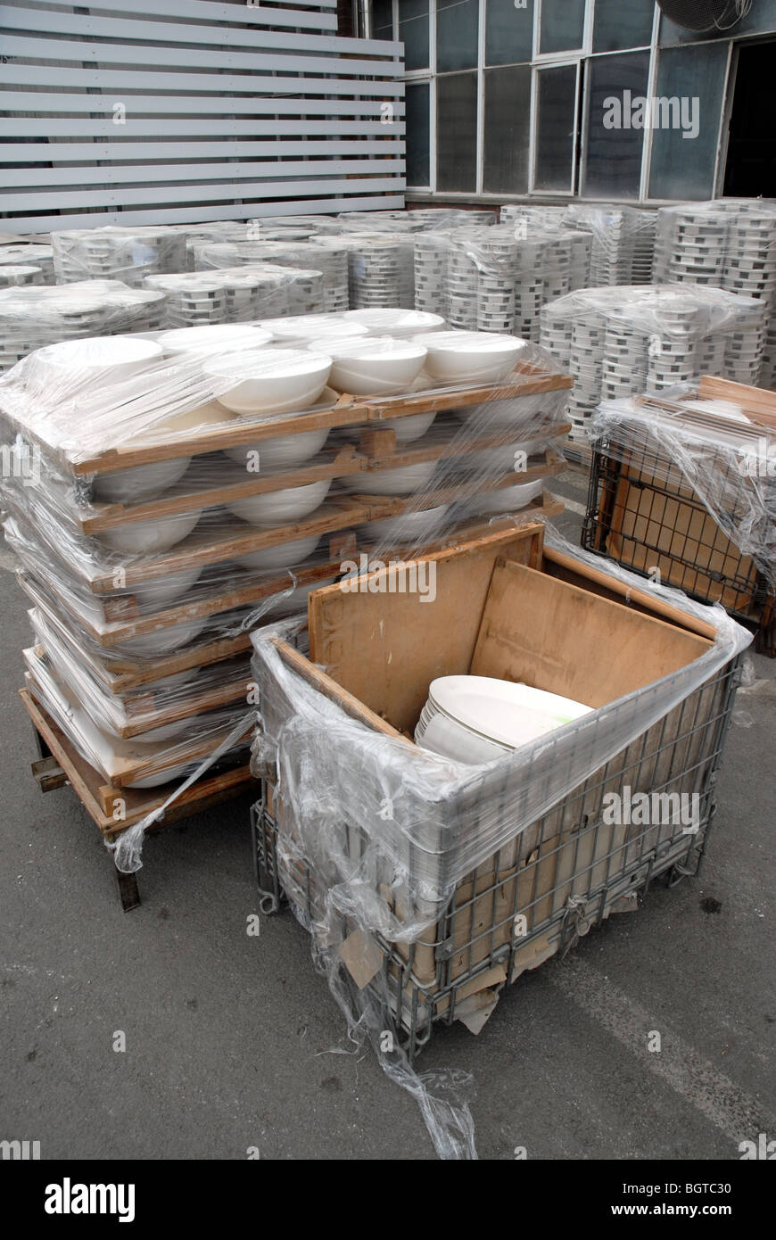 Pallets and stacks of plates and other pottery crockery, outside a ...
