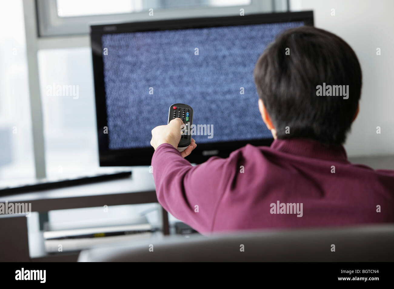 Back shot of man watching TV and holding remote Stock Photo - Alamy